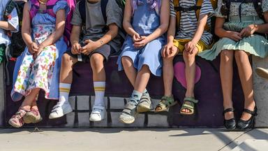 Kinder sitzen auf einer Mauer.